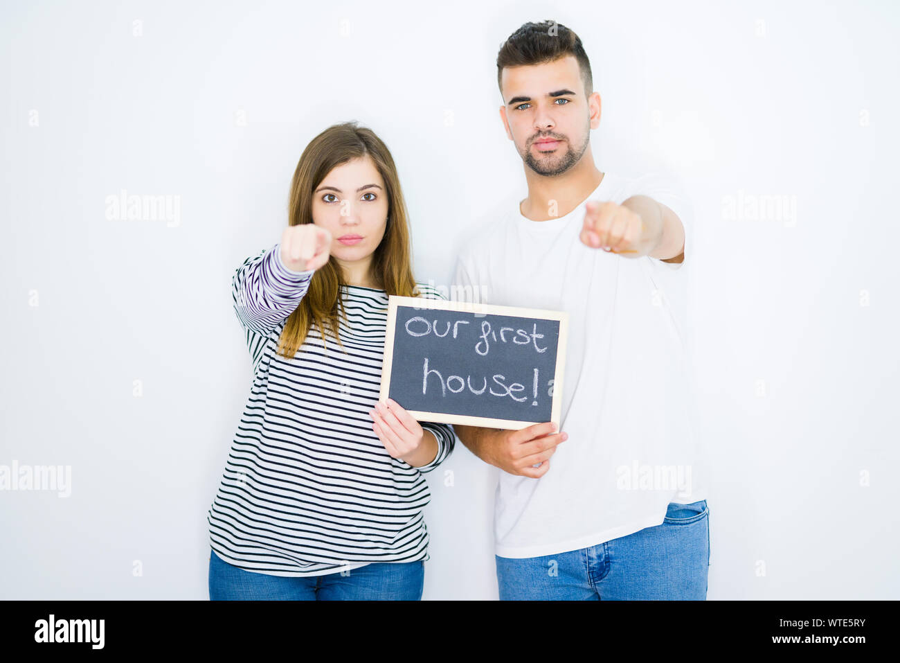 Young couple holding blackboard with our first home text over white ...