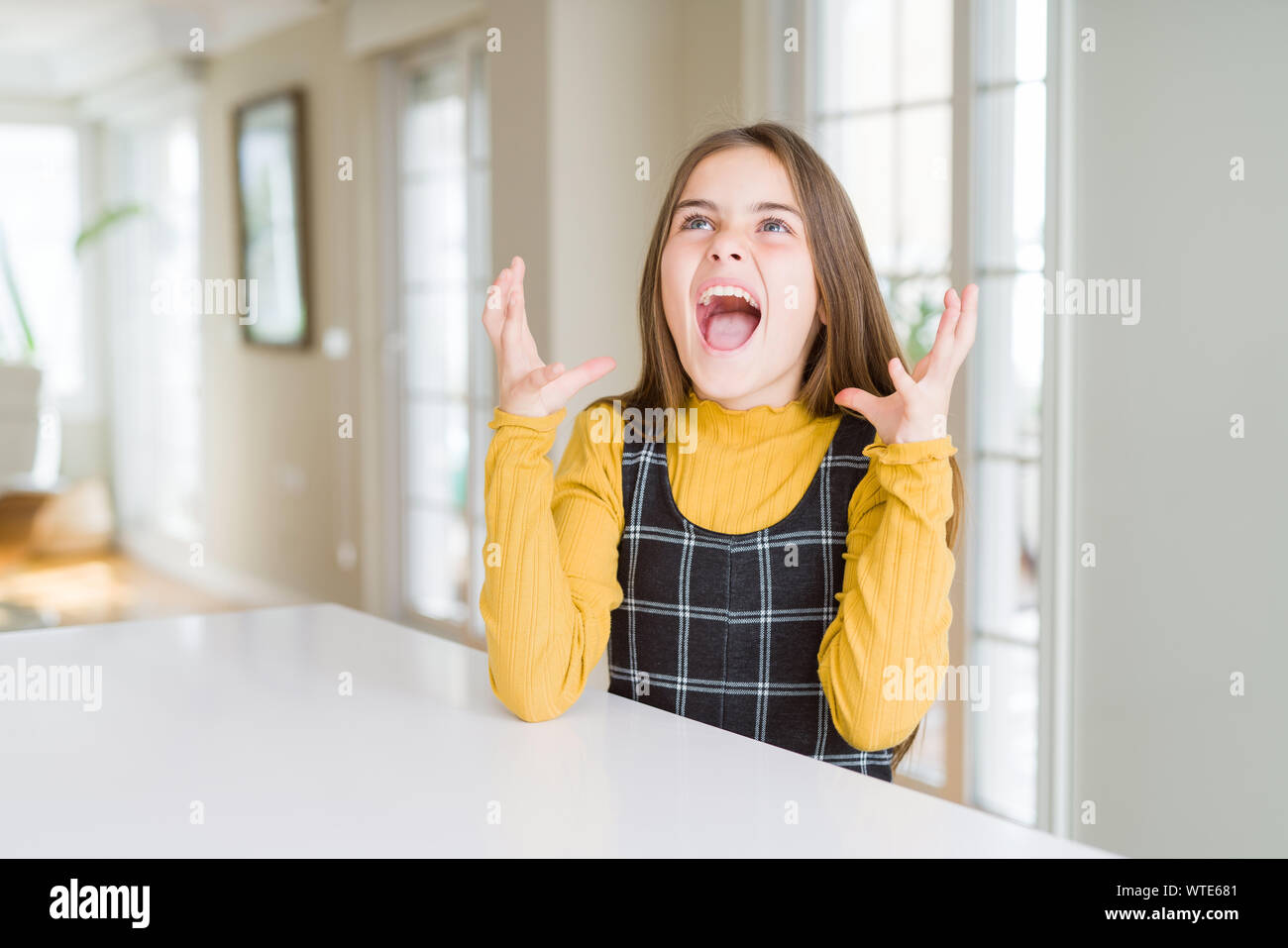 Beautiful young girl kid sitting on the table crazy and mad shouting ...