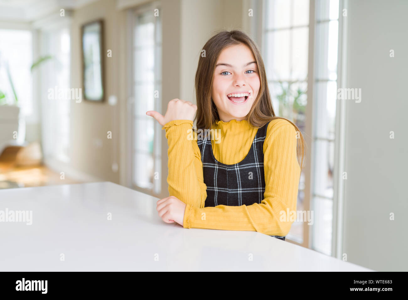 Beautiful young girl kid sitting on the table smiling with happy face ...