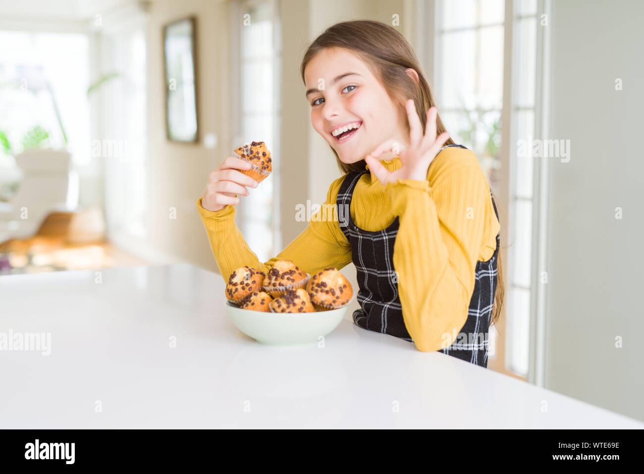 Beautiful young girl eating chocolate chips muffins doing ok sign with ...