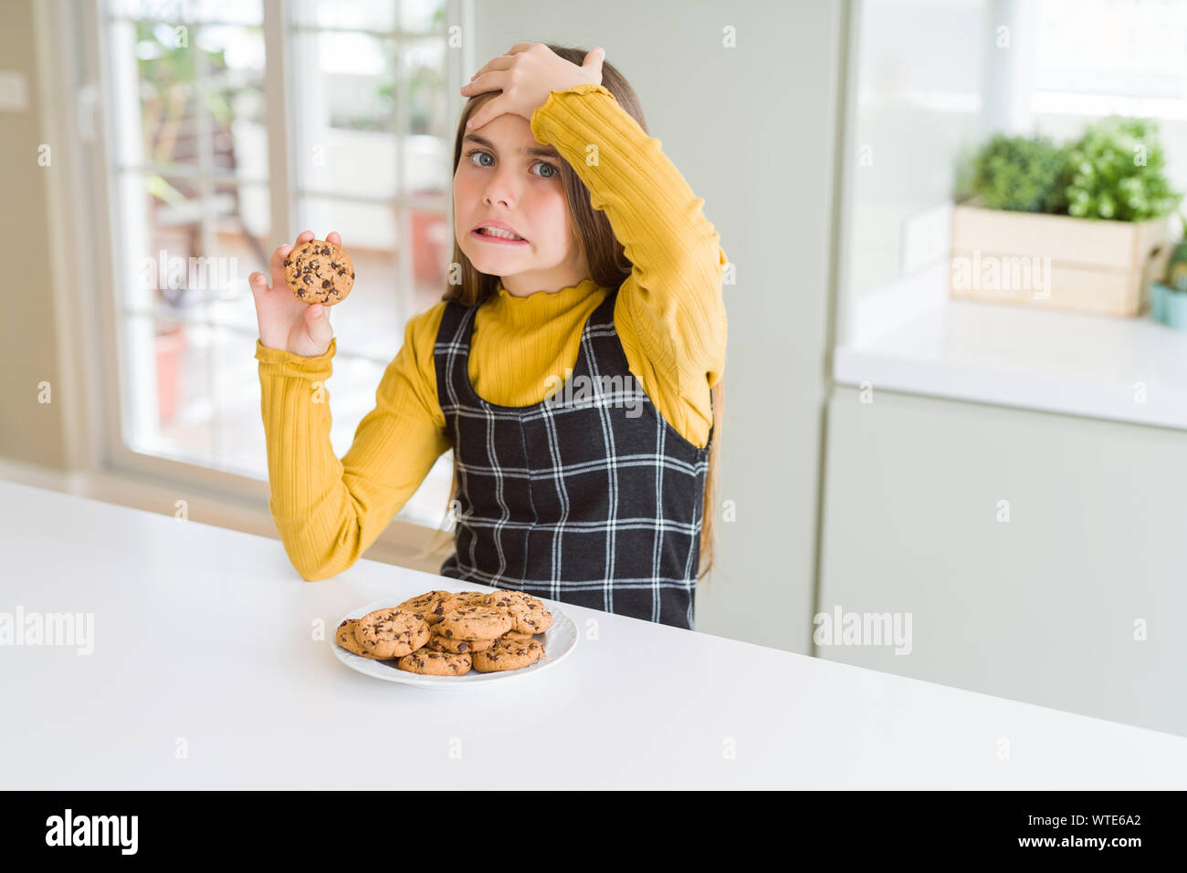 Beautiful young girl kid eating chocolate chips cookies stressed with ...