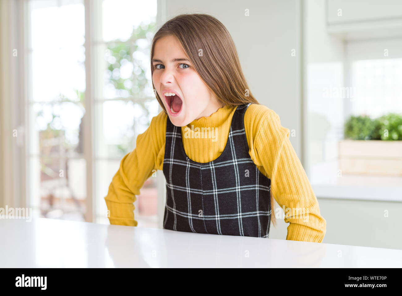 Young beautiful blonde kid girl wearing casual yellow sweater at home angry and mad screaming ...