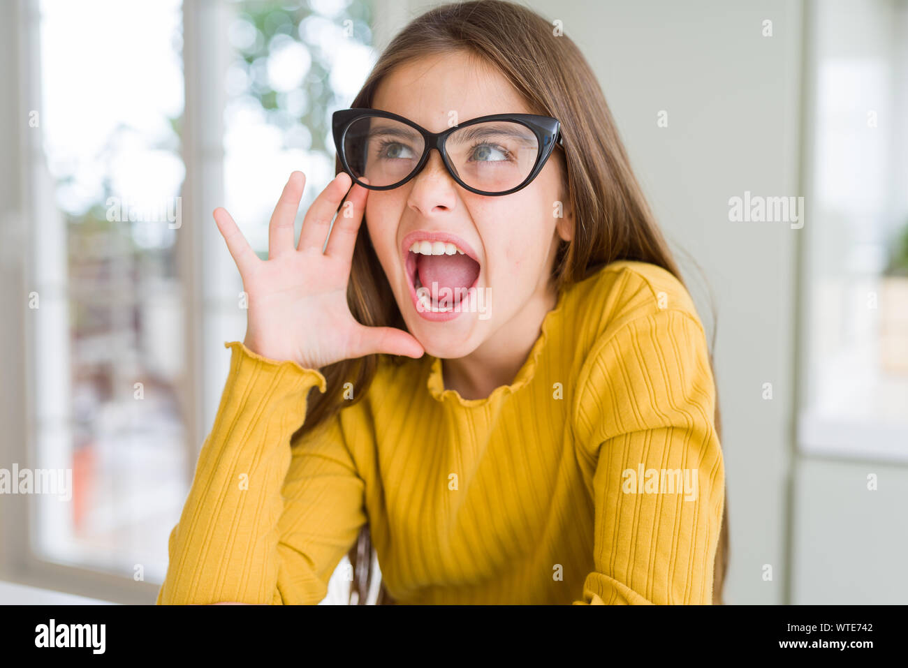 Beautiful young girl kid wearing glasses shouting and screaming loud to ...