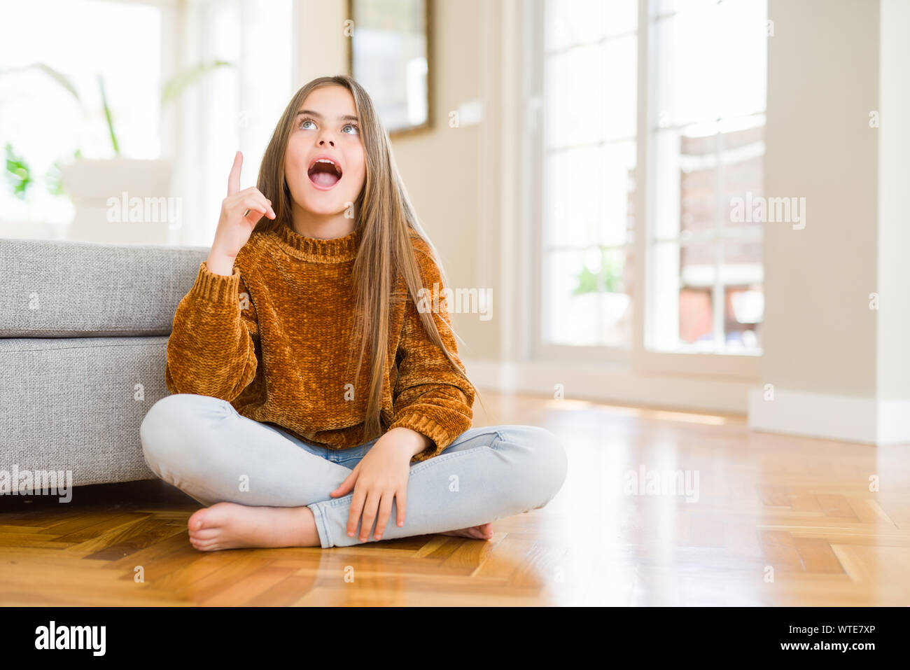 Beautiful young girl kid sitting on the floor at home pointing finger ...