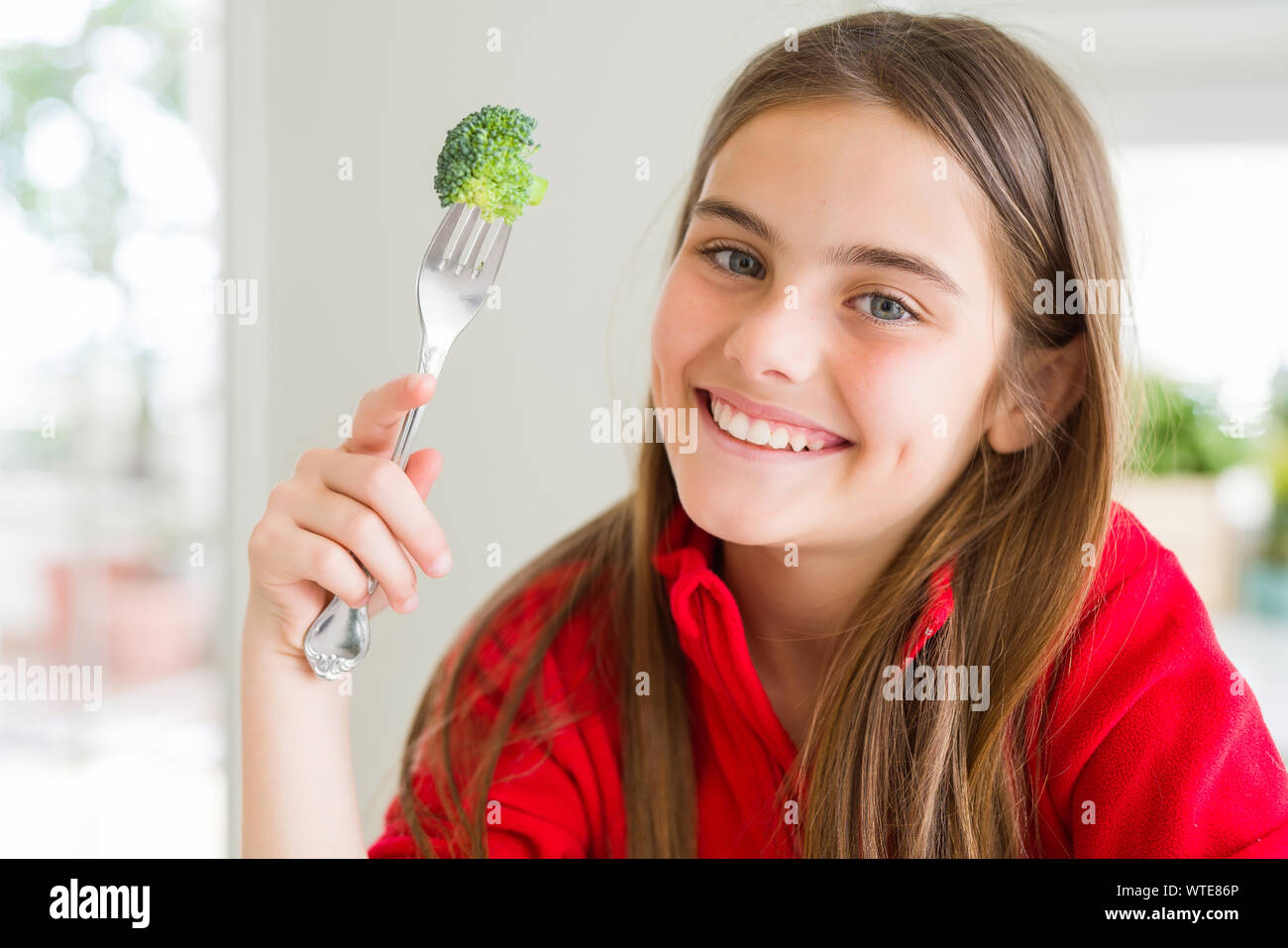 Beautiful young girl eating fresh broccoli with a happy face standing ...