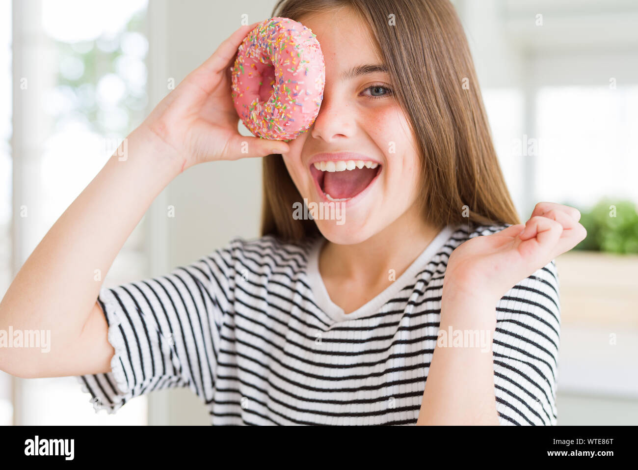 Beautiful young girl kid eating sweet pink donut screaming proud and ...