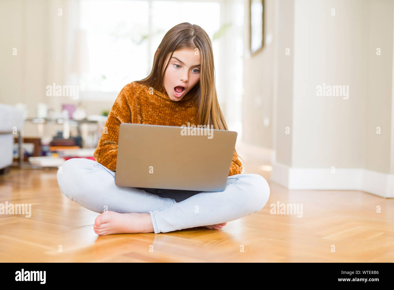 Beautiful young girl studying using laptop sitting on the floor at home ...
