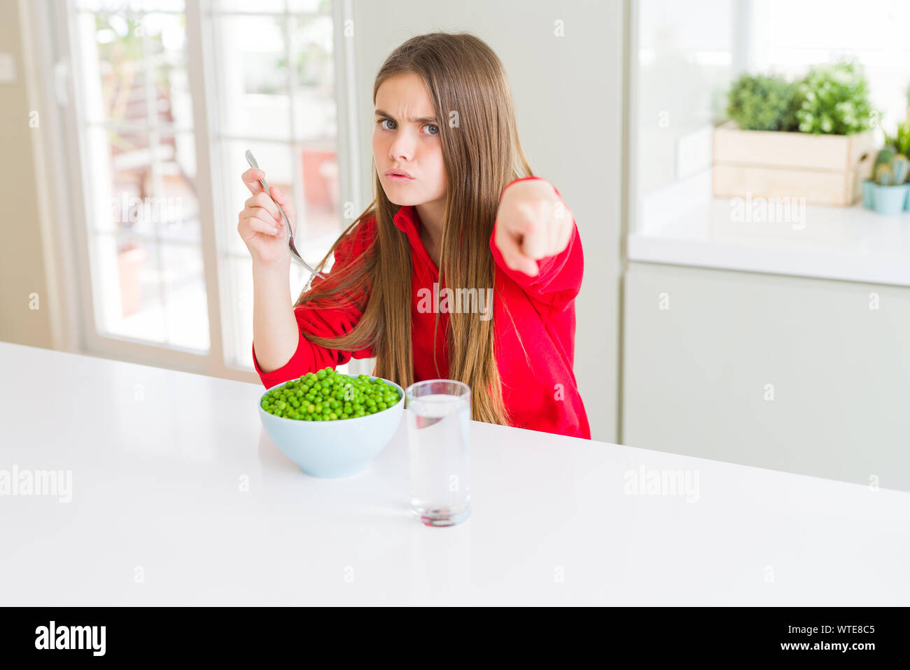 Beautiful young girl eating healthy green peas pointing with finger to ...