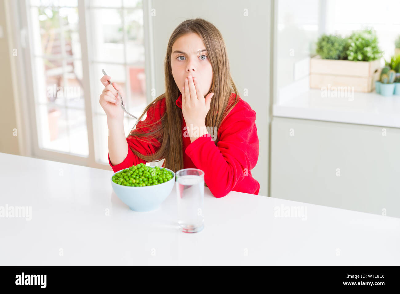Beautiful young girl eating healthy green peas cover mouth with hand ...