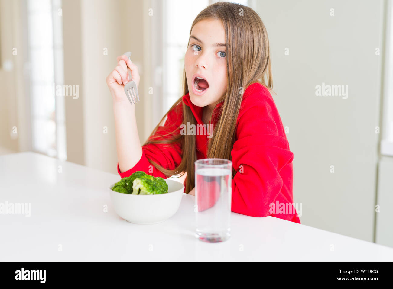 Beautiful young girl kid eating fresh broccoli and drinking water ...
