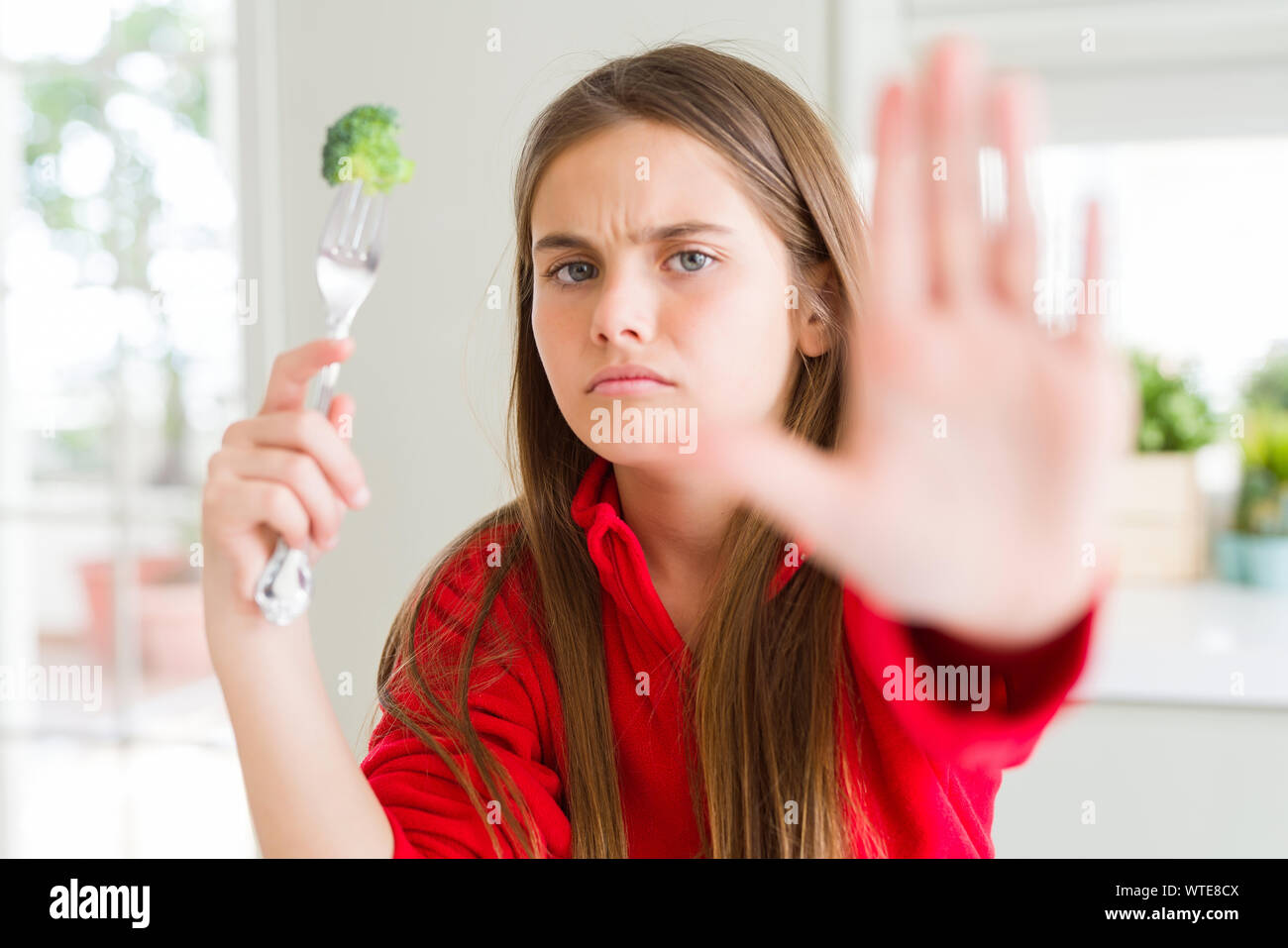 Beautiful young girl eating fresh broccoli with open hand doing stop ...