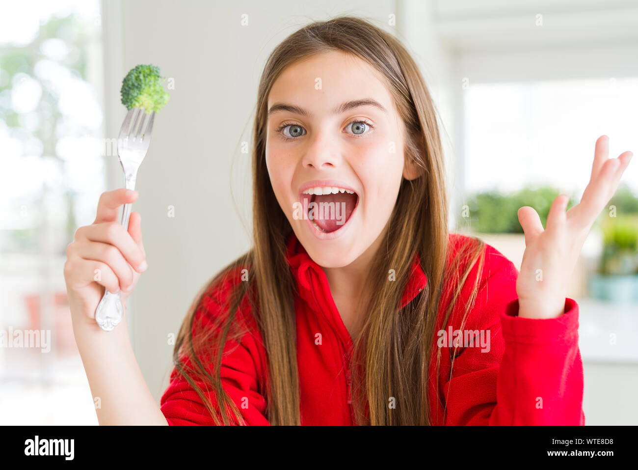 Beautiful young girl eating fresh broccoli very happy and excited ...