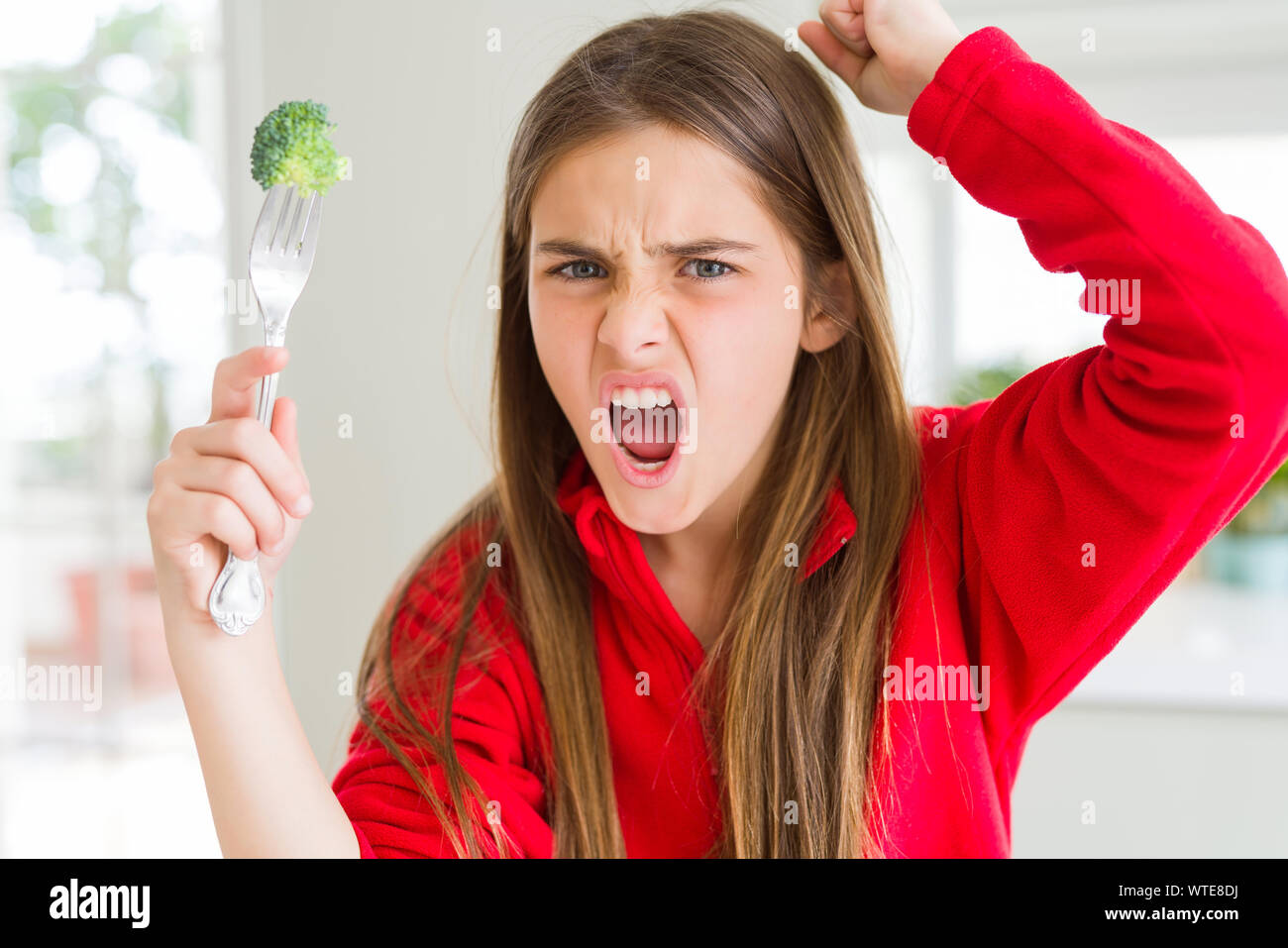 Beautiful young girl eating fresh broccoli annoyed and frustrated ...