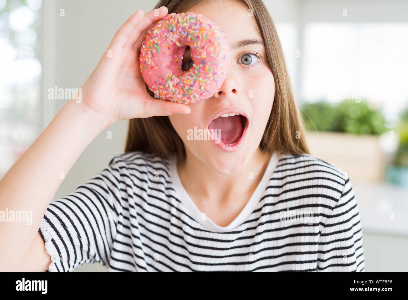 Beautiful young girl kid eating sweet pink donut scared in shock with a ...