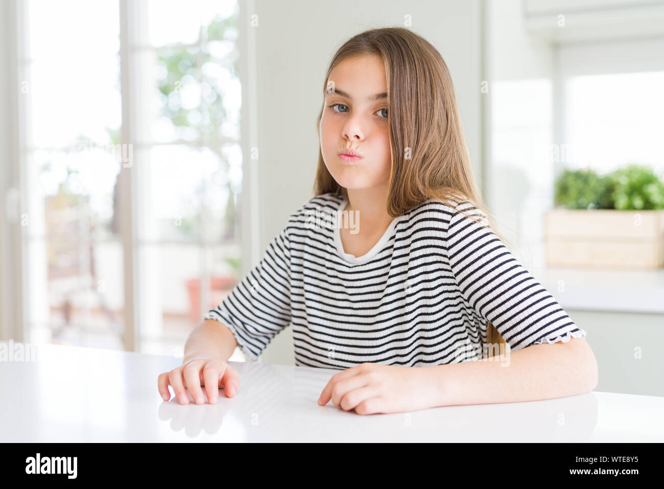 Beautiful young girl kid wearing stripes t-shirt puffing cheeks with ...