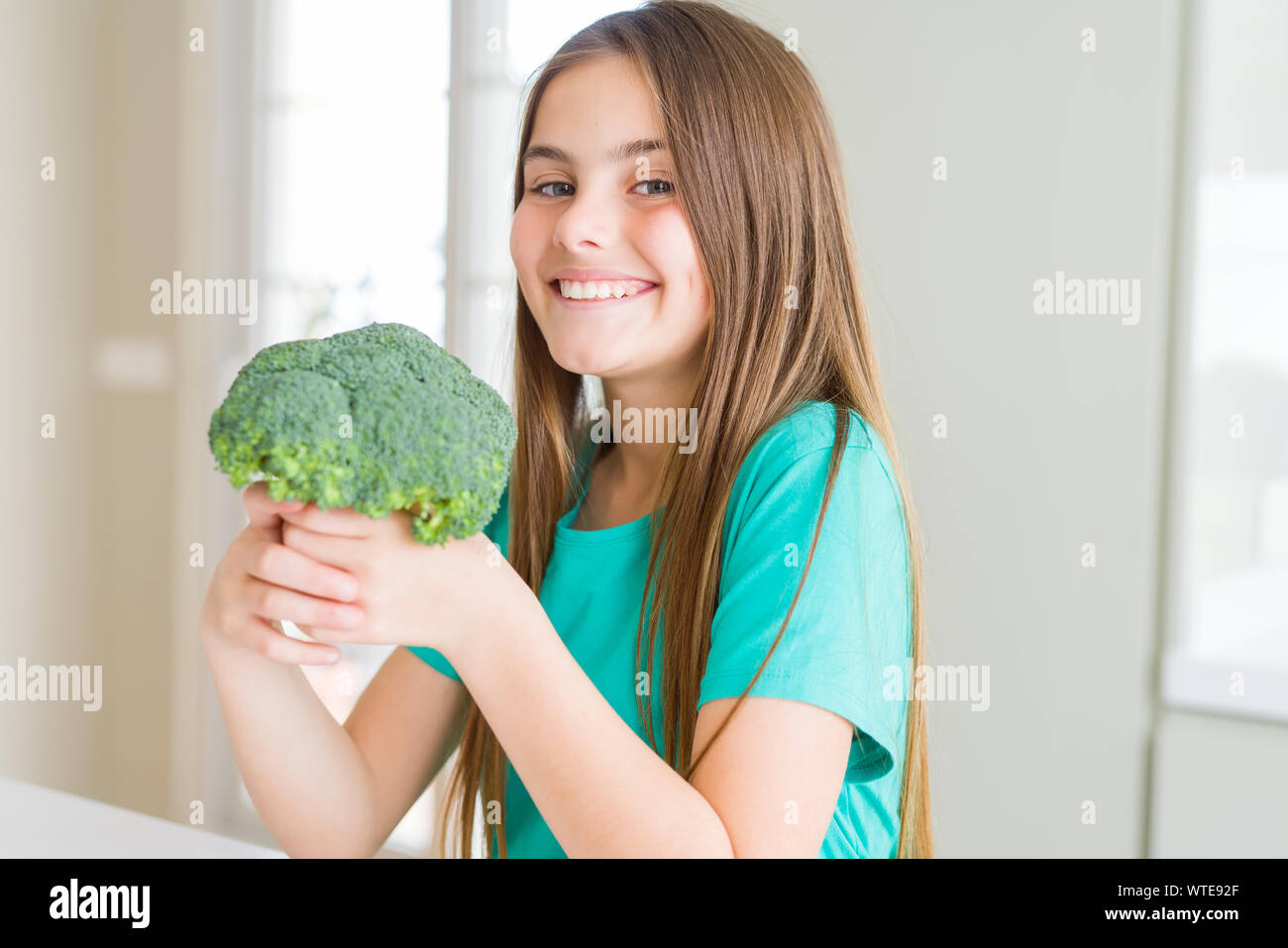 Beautiful young girl eating fresh broccoli with a happy face standing ...