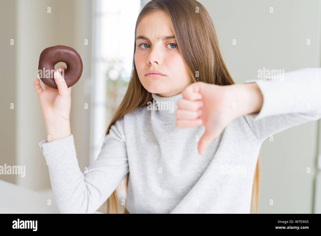 Beautiful young girl wearing eating a chocolate donut with angry face ...