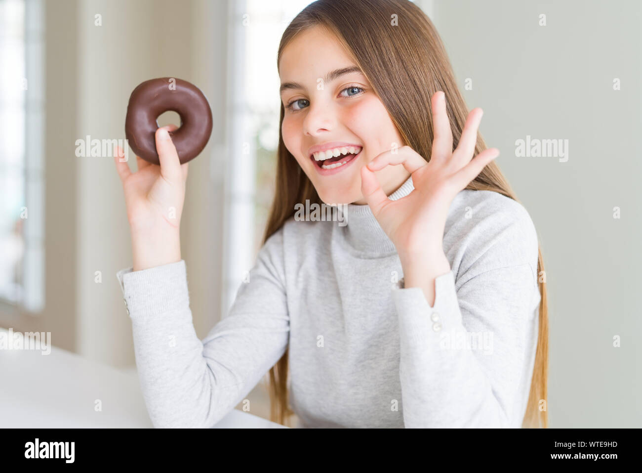 Beautiful young girl wearing eating a chocolate donut doing ok sign ...