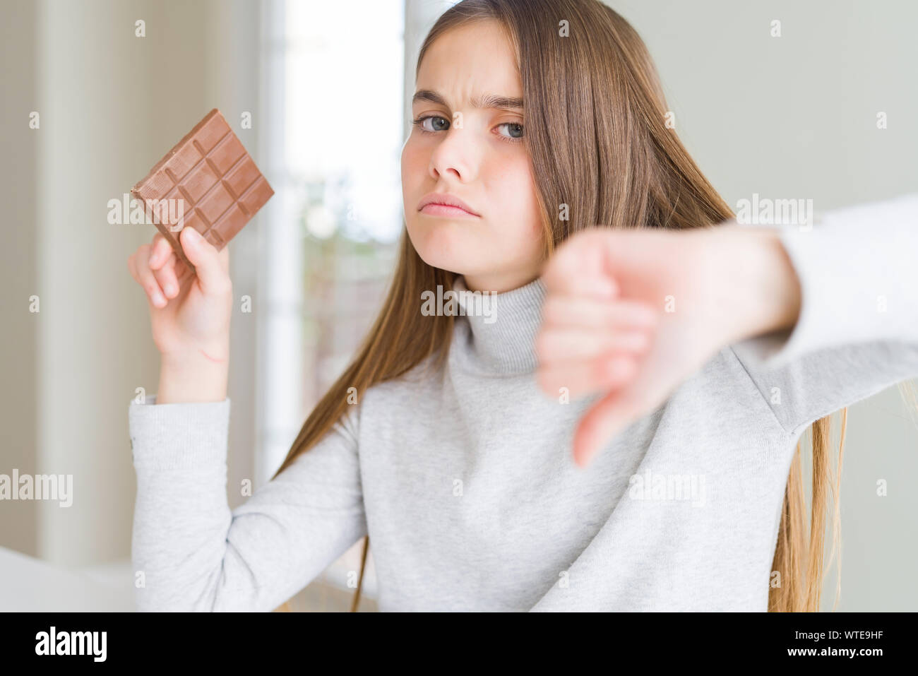Beautiful young girl kid eating chocolate bar with angry face, negative ...