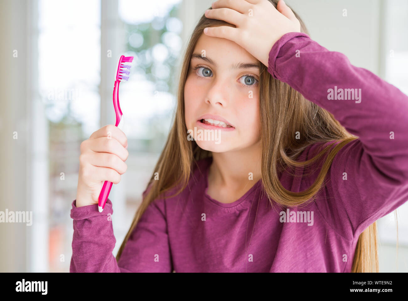 Beautiful young girl kid holding pink dental toothbrush stressed with ...