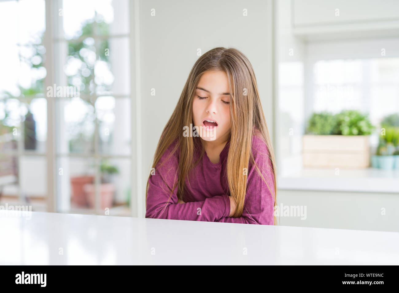 Beautiful young girl kid on white table with hand on stomach because ...
