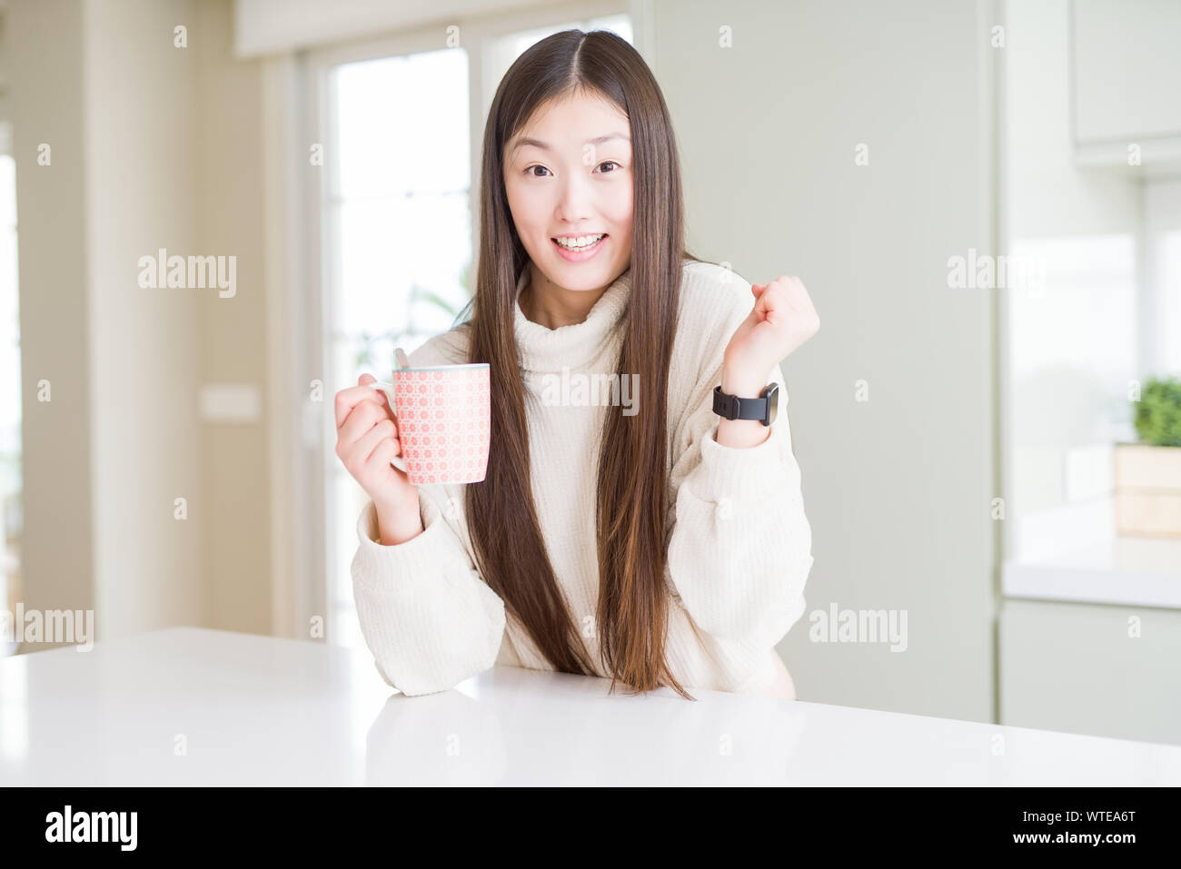 Beautiful Asian woman drinking a cup of coffee screaming proud and ...