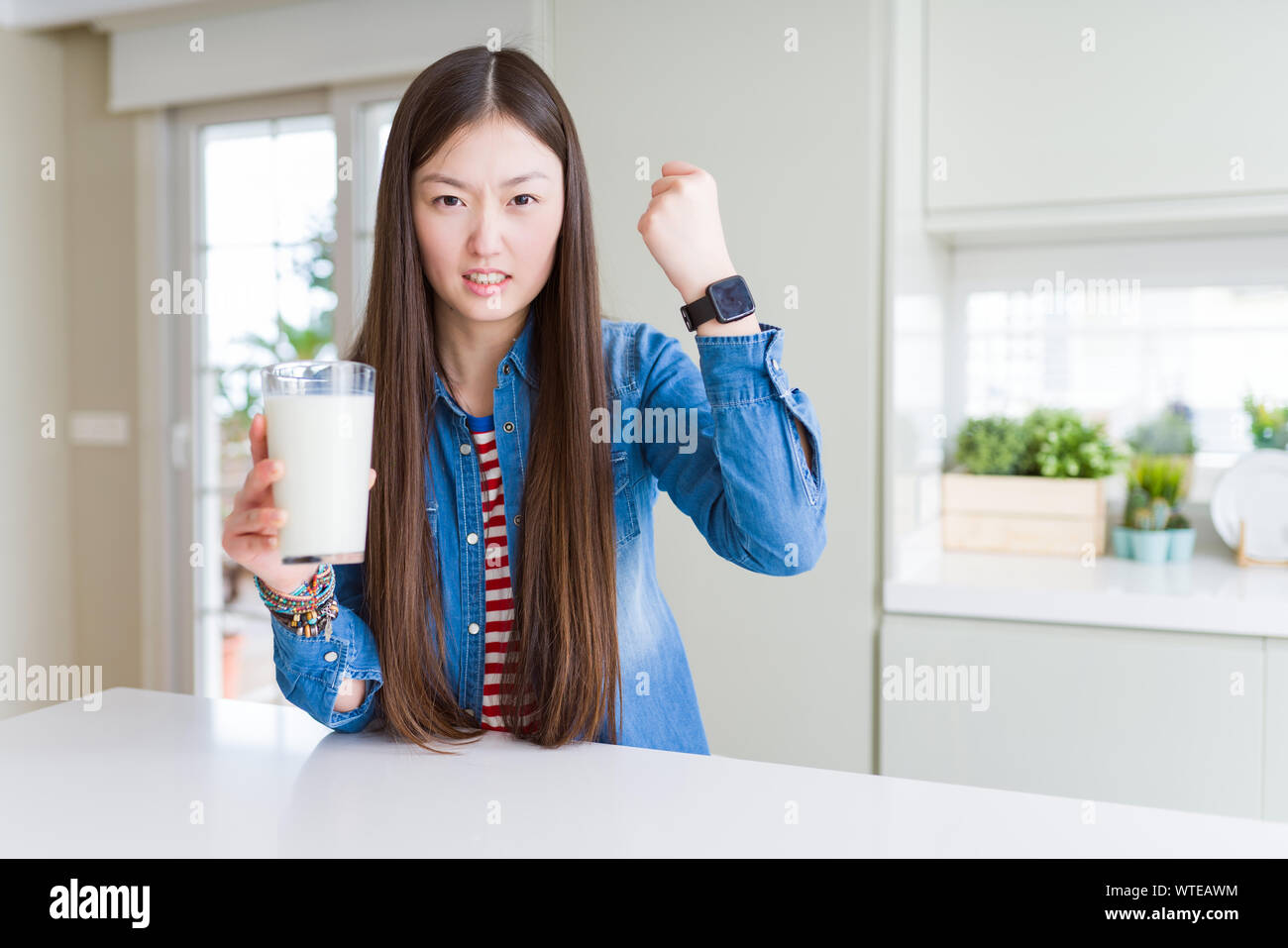 Beautiful Asian woman drinking a fresh glass of milk annoyed and ...
