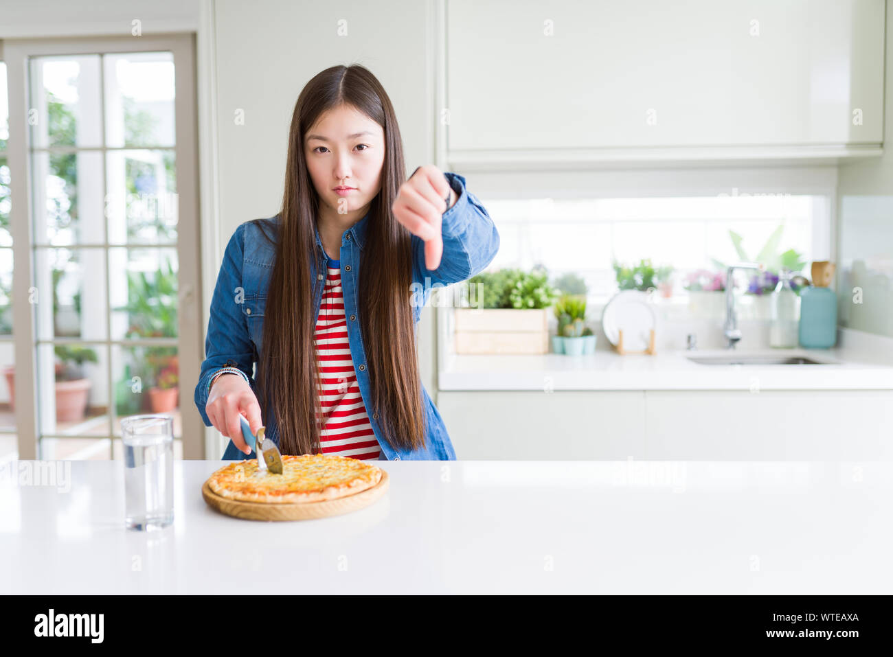 Beautiful Asian woman eating and cutting chesse pizza with angry face ...