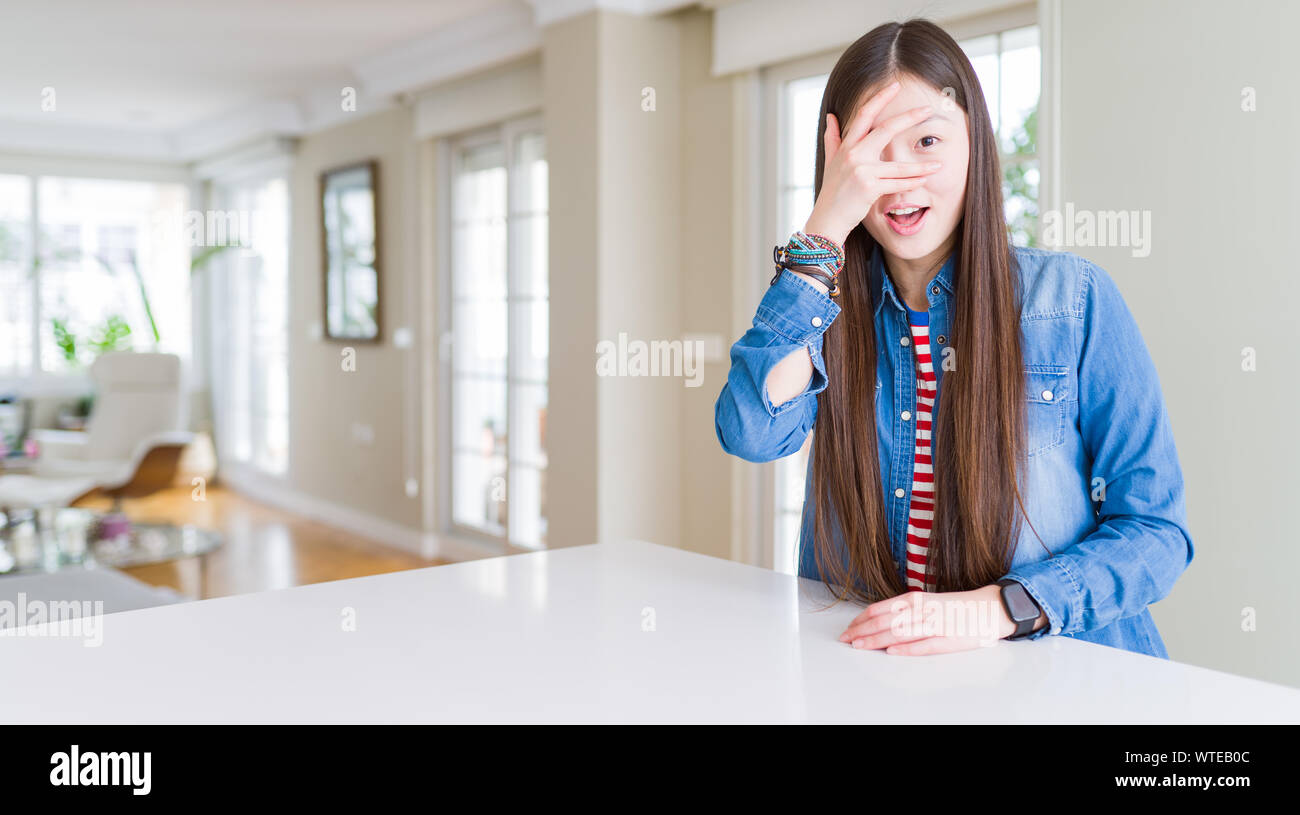 Young beautiful asian woman with long hair wearing denim jacket peeking ...