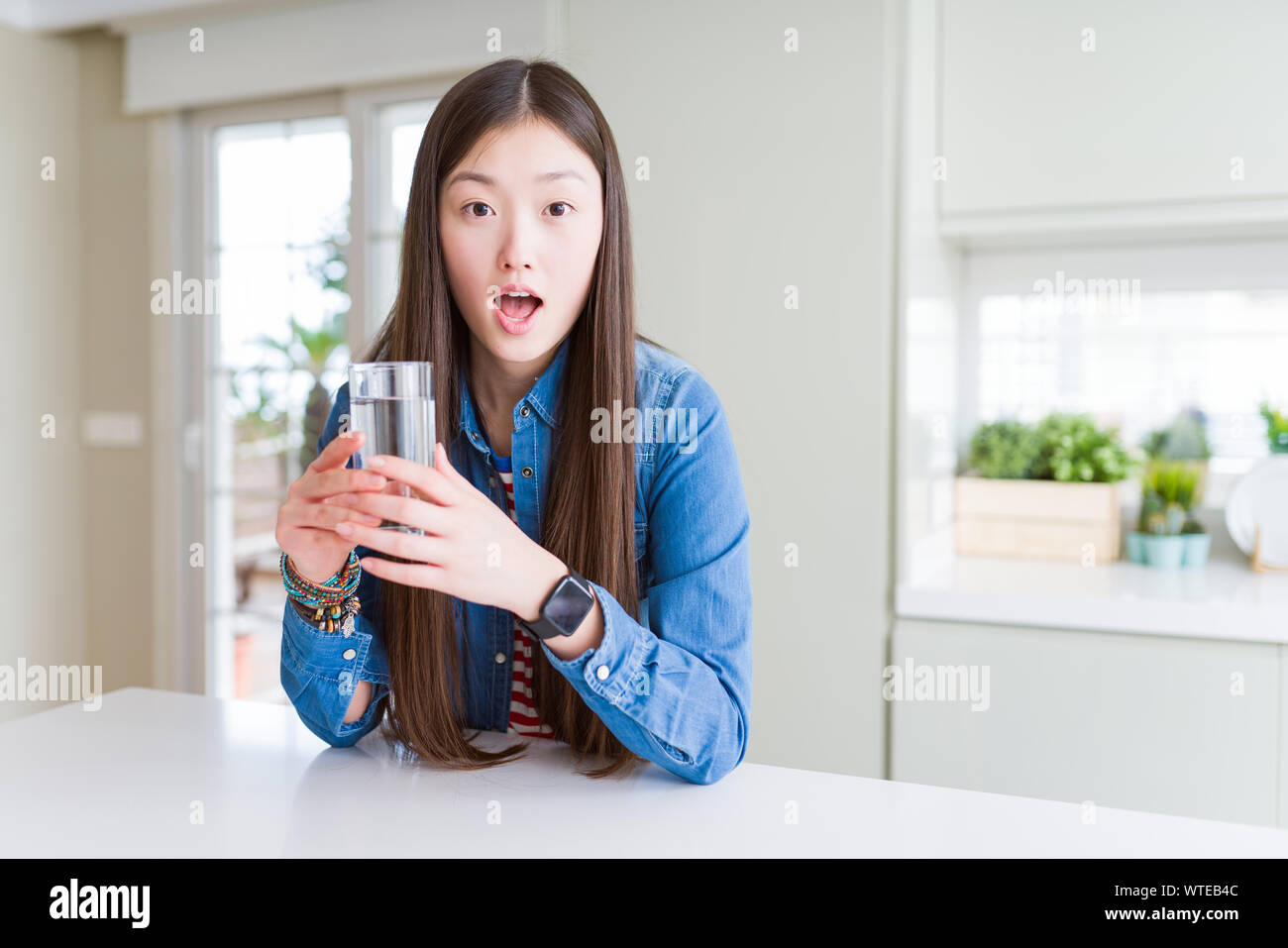 Beautiful Asian woman drinking a glass of fresh water scared in shock ...