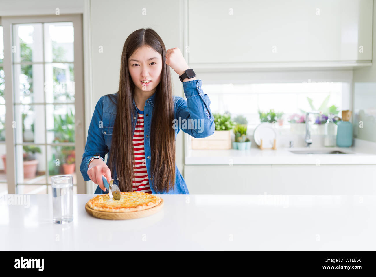 Beautiful Asian woman eating and cutting chesse pizza annoyed and ...
