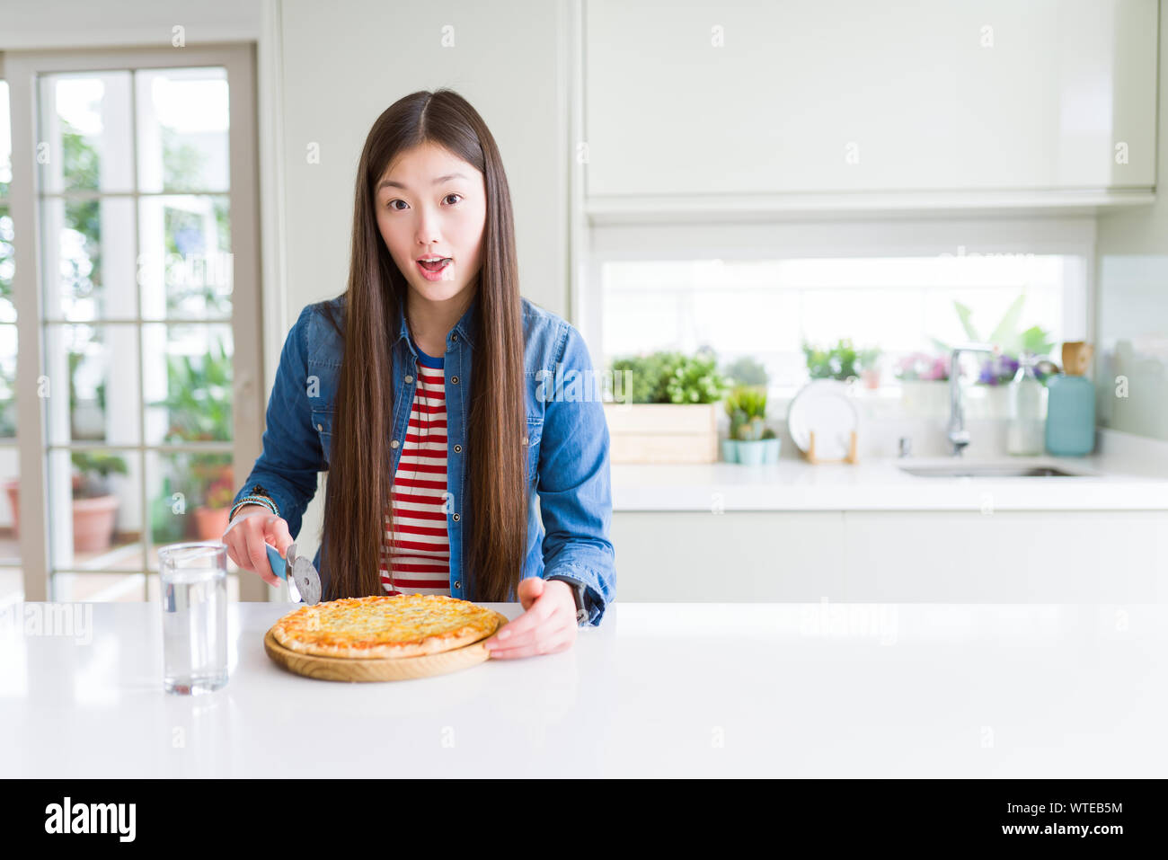 Beautiful Asian woman eating and cutting chesse pizza scared in shock ...