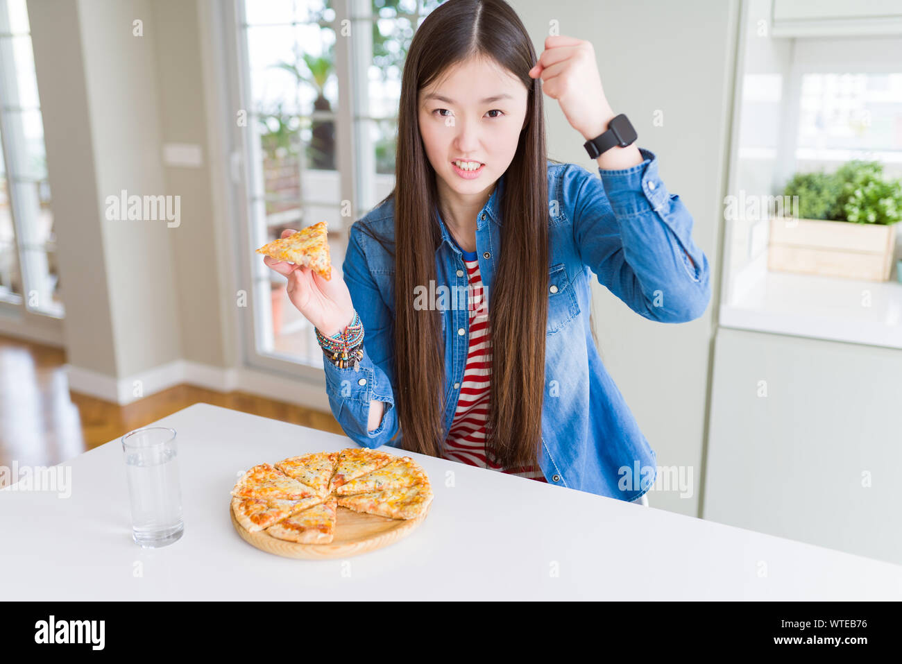 Beautiful Asian woman eating a slice of cheese pizza annoyed and ...