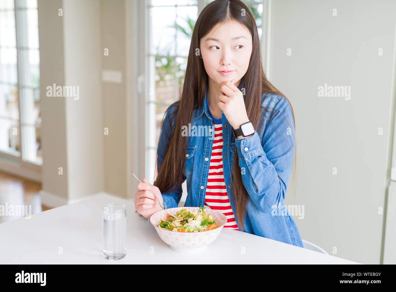 Beautiful Asian woman eating healthy pasta salad serious face thinking ...