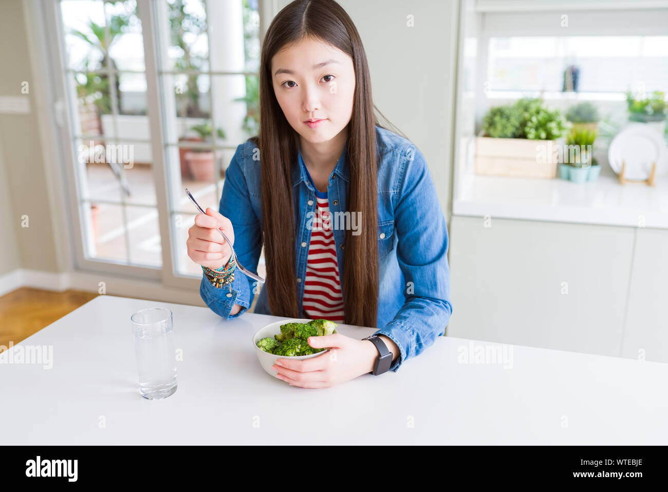 Beautiful Asian woman eating green fresh broccoli with a confident ...