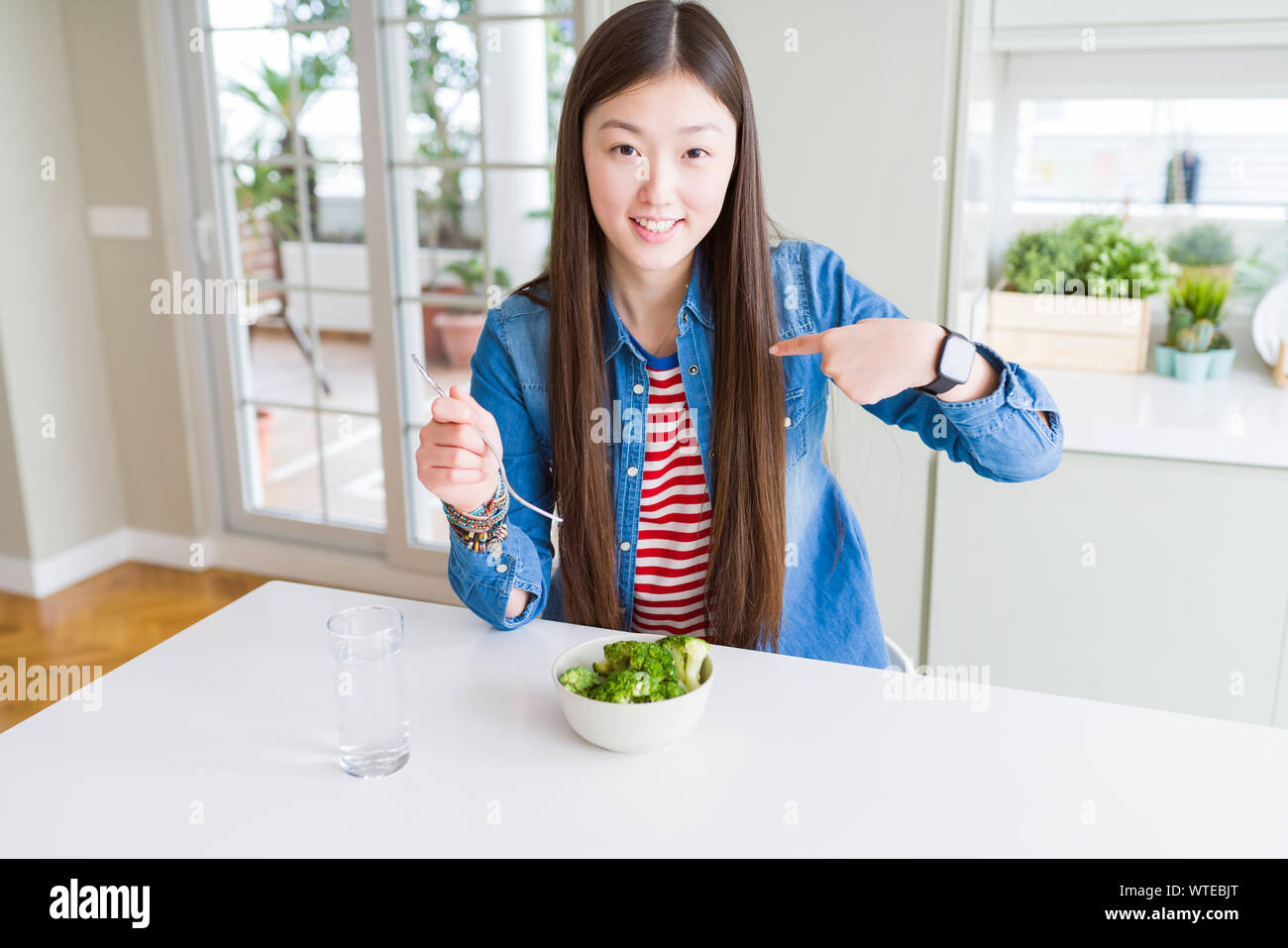 Beautiful Asian woman eating green fresh broccoli with surprise face ...