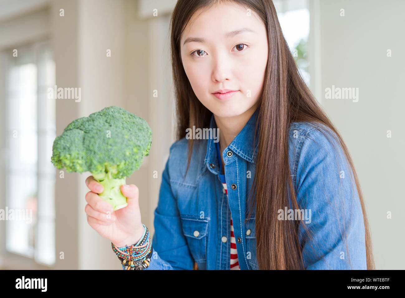 Beautiful Asian woman eating green fresh broccoli with a confident ...