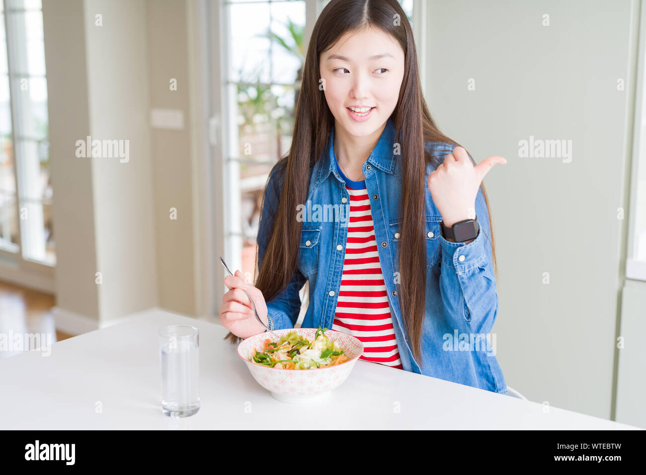 Beautiful Asian woman eating healthy pasta salad pointing and showing ...