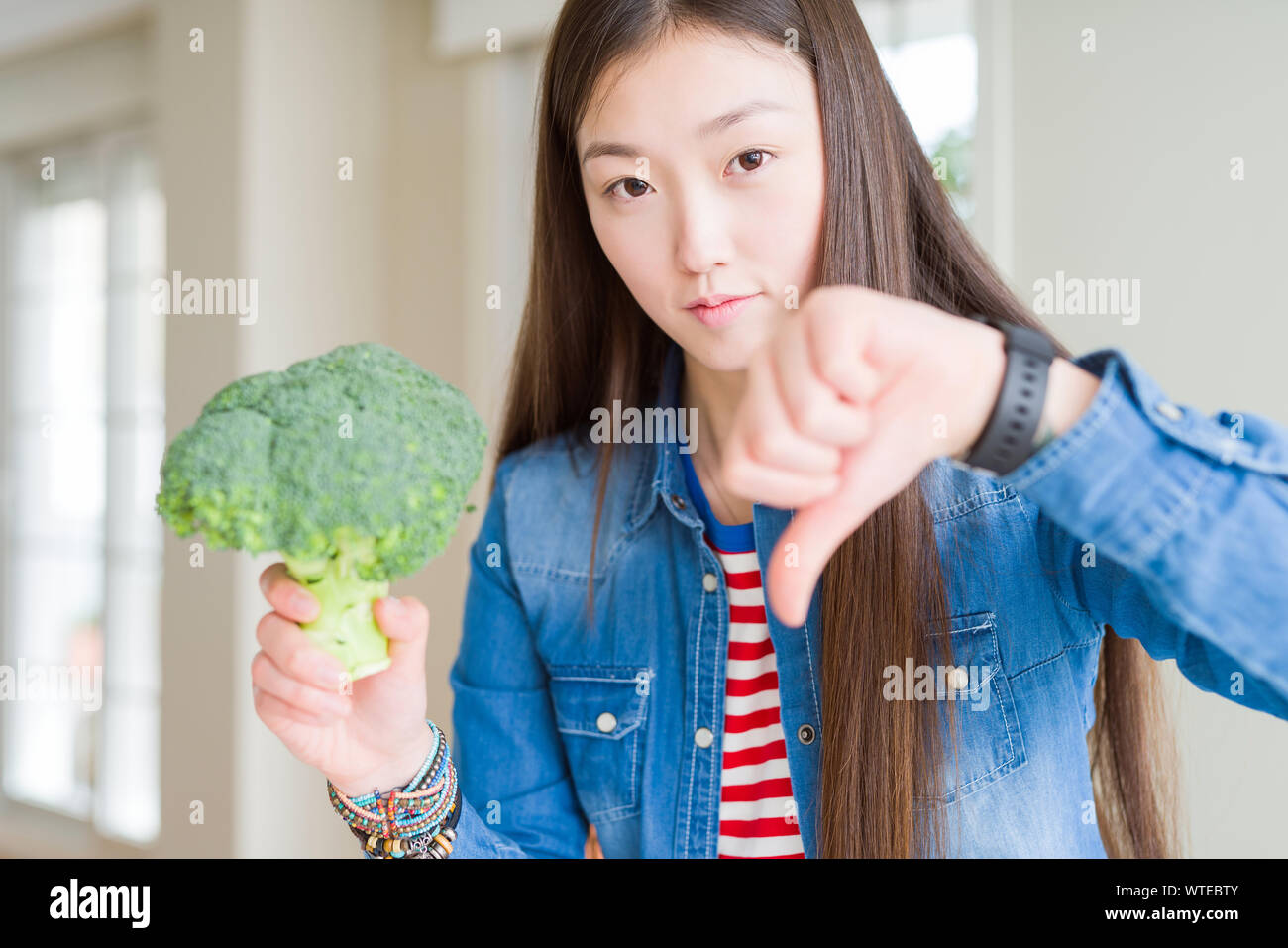 Beautiful Asian woman eating green fresh broccoli with angry face ...