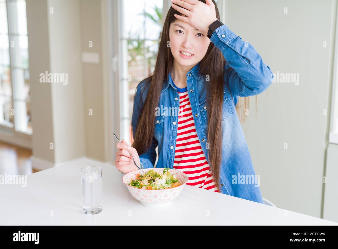 Beautiful Asian woman eating healthy pasta salad stressed with hand on ...