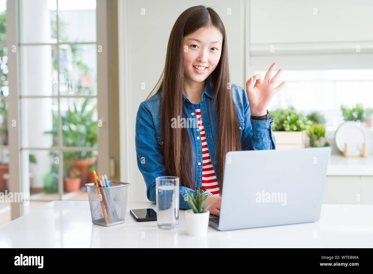 Beautiful Asian woman working using computer laptop doing ok sign with ...