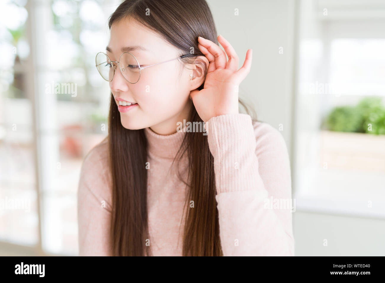 Beautiful Asian woman wearing glasses smiling with hand over ear ...