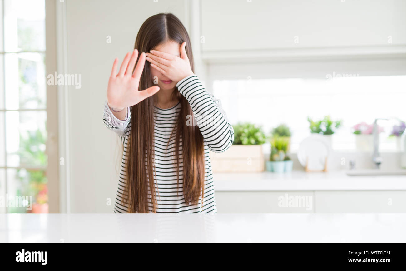Beautiful Asian woman wearing stripes sweater covering eyes with hands ...