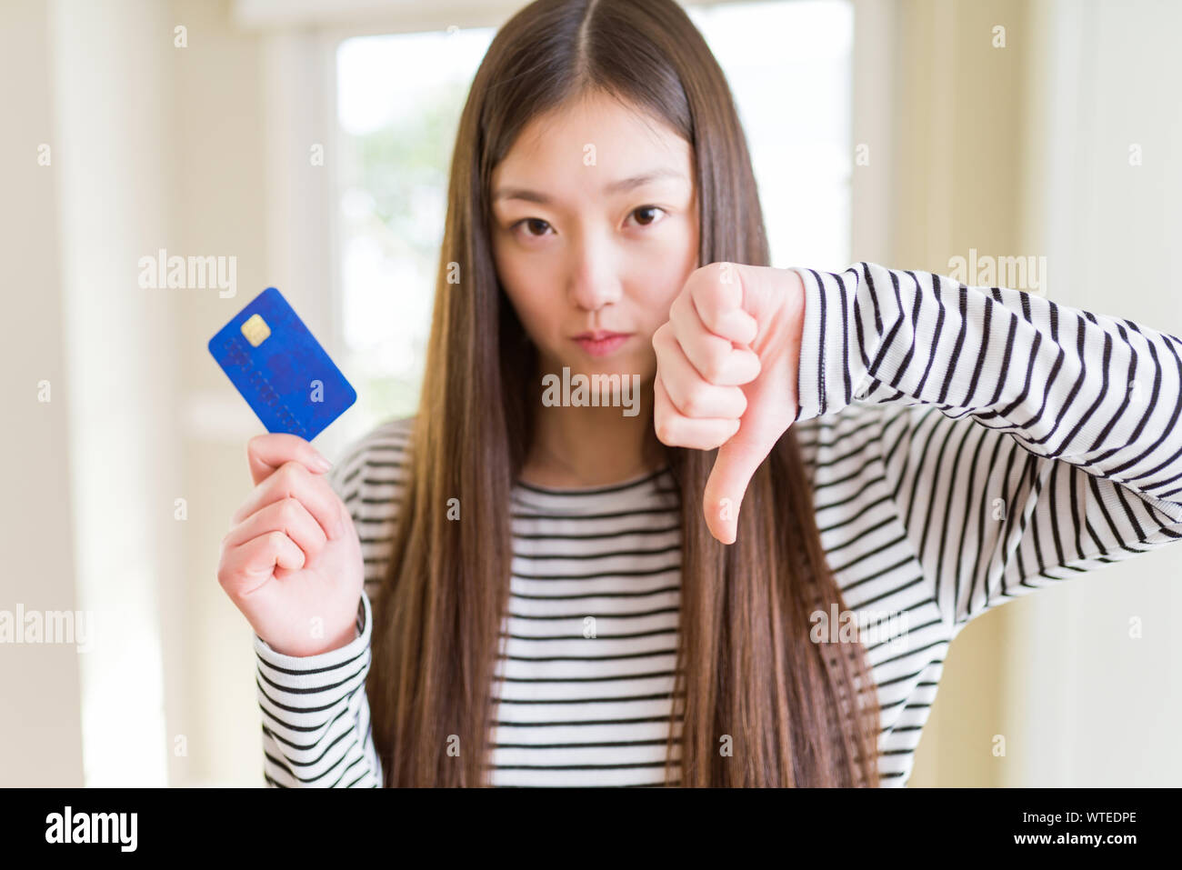 Beautiful Asian woman holding credit card with angry face, negative ...