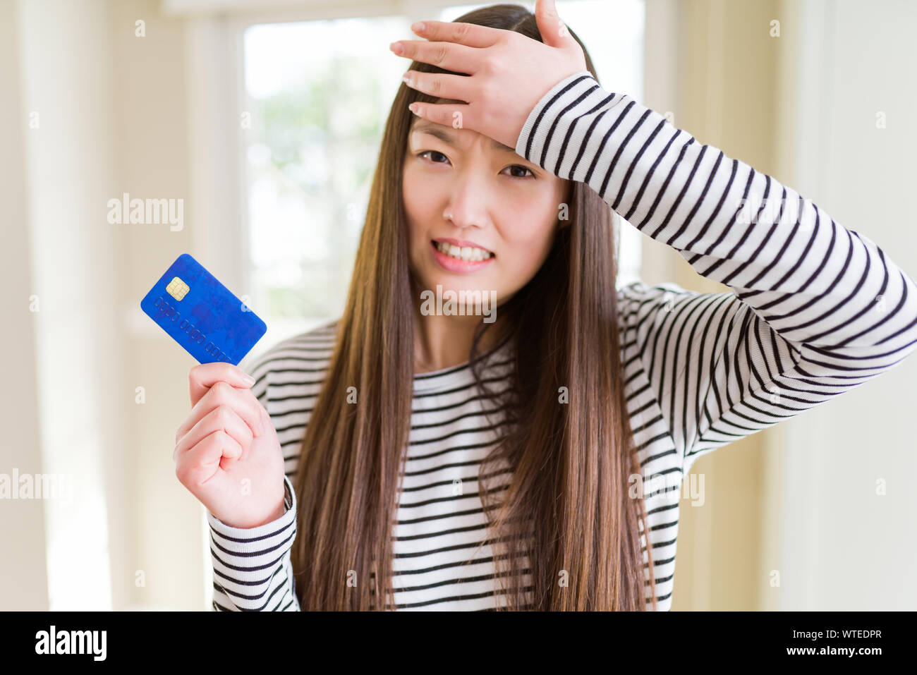 Beautiful Asian woman holding credit card stressed with hand on head ...