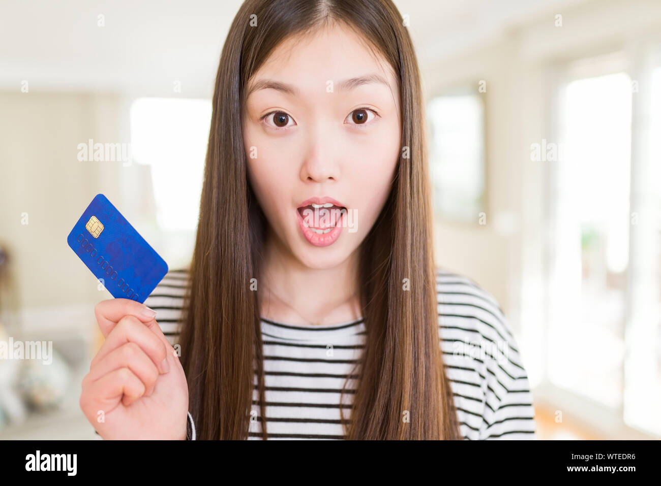 Beautiful Asian woman holding credit card scared in shock with a ...