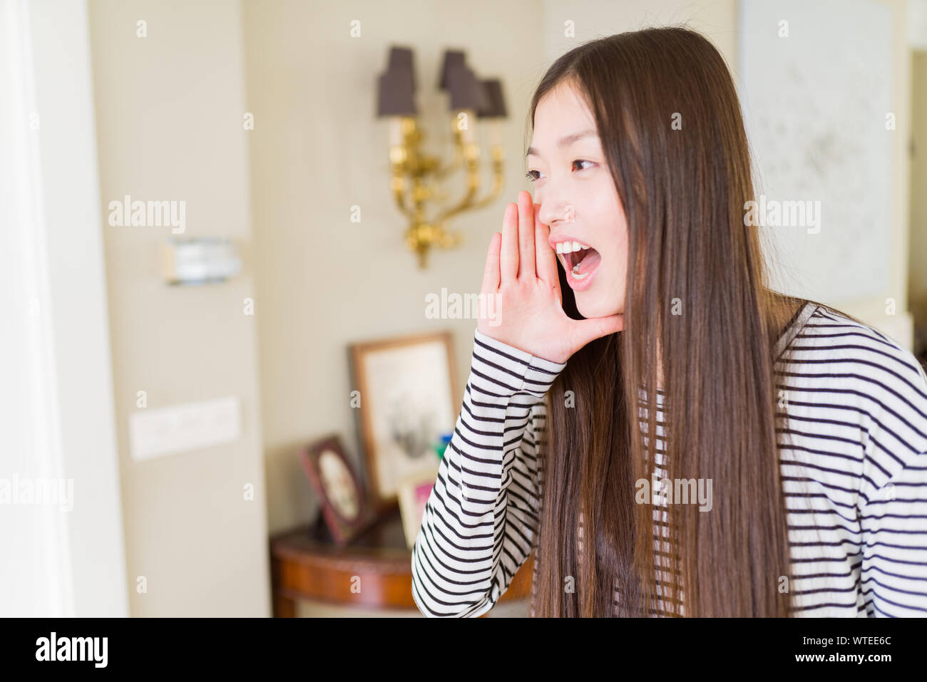 Beautiful Asian woman wearing stripes sweater over living room ...