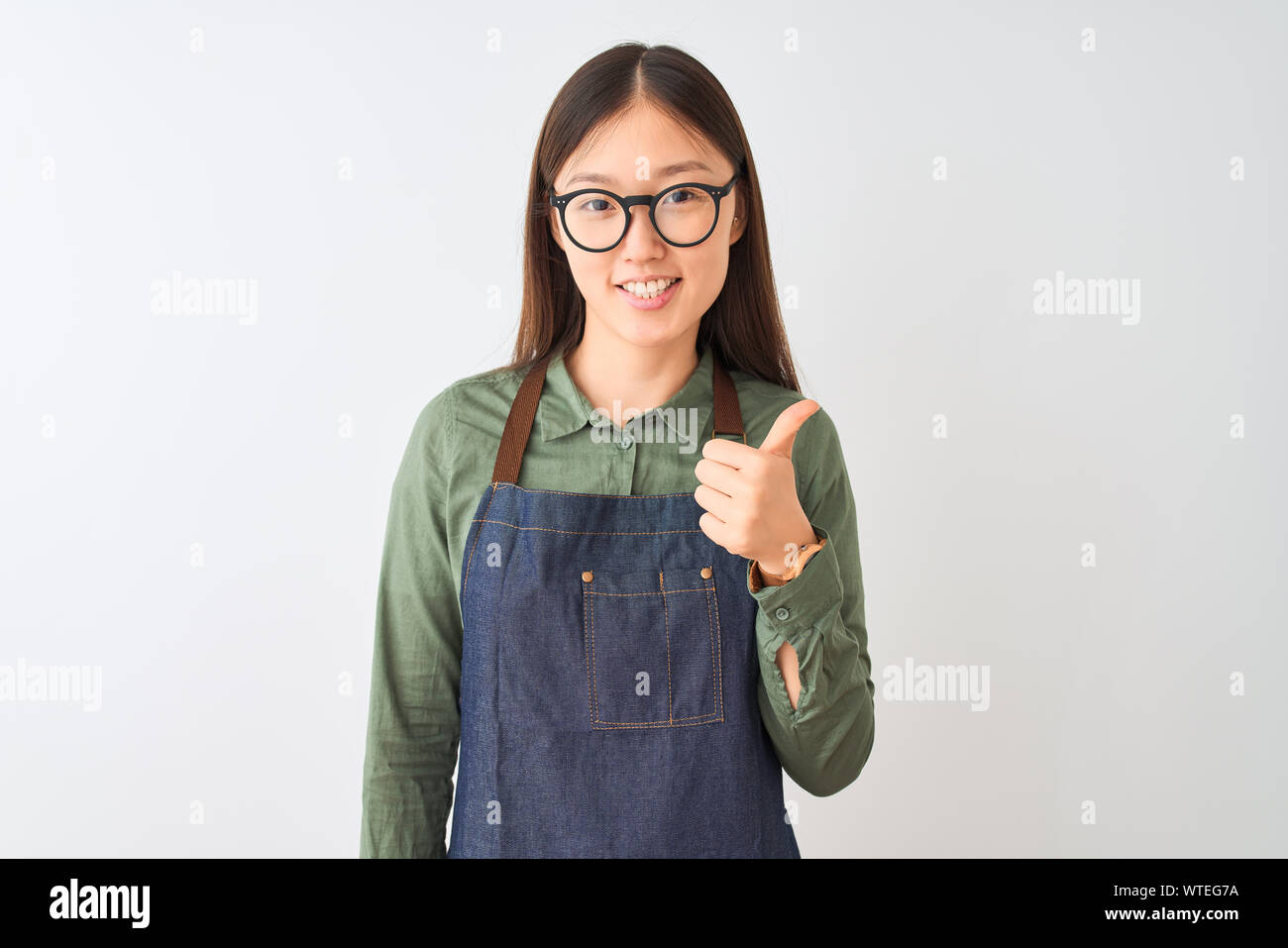 Young chinese shopkeeper woman wearing apron and glasses over isolated ...