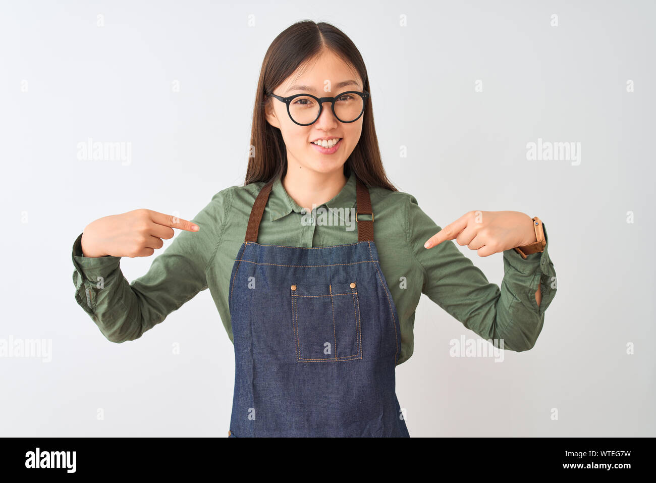 Young chinese shopkeeper woman wearing apron and glasses over isolated ...