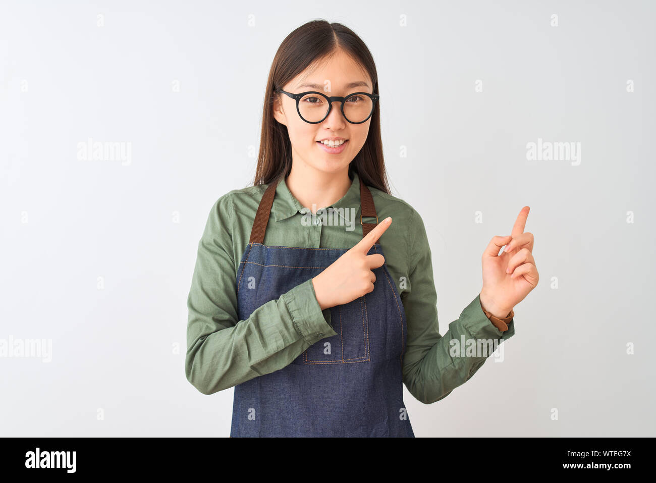 Young chinese shopkeeper woman wearing apron and glasses over isolated ...